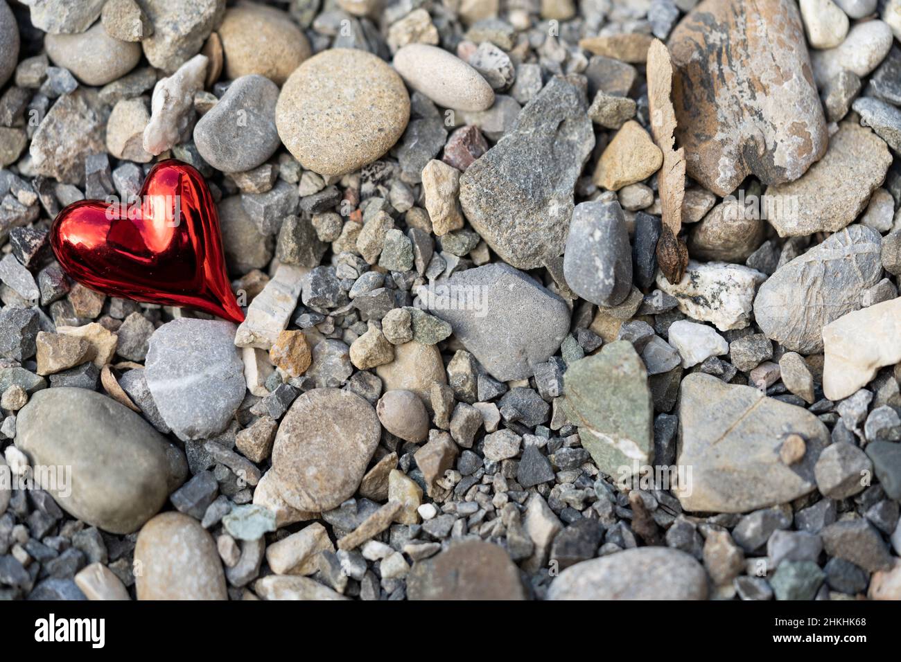 top view of red shiny heart in middle of colorful pebble stones outdoor ...