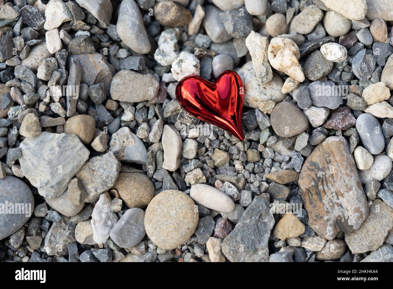 top view of red shiny heart in middle of colorful pebble stones outdoor ...