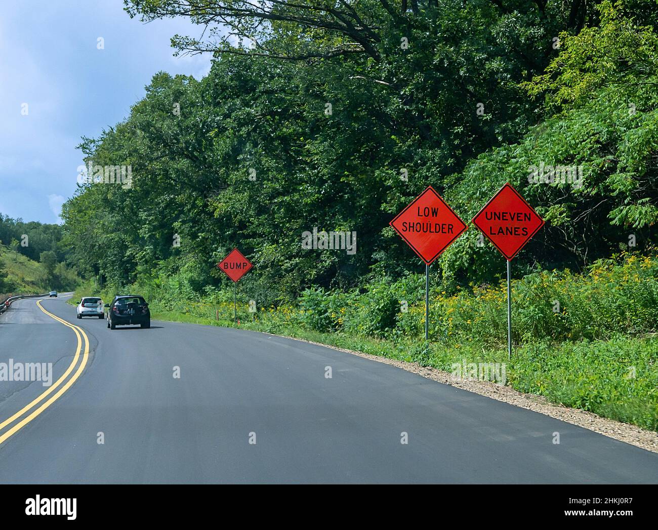 Orange warning signs along curvy asphalt highway with cars on road ...