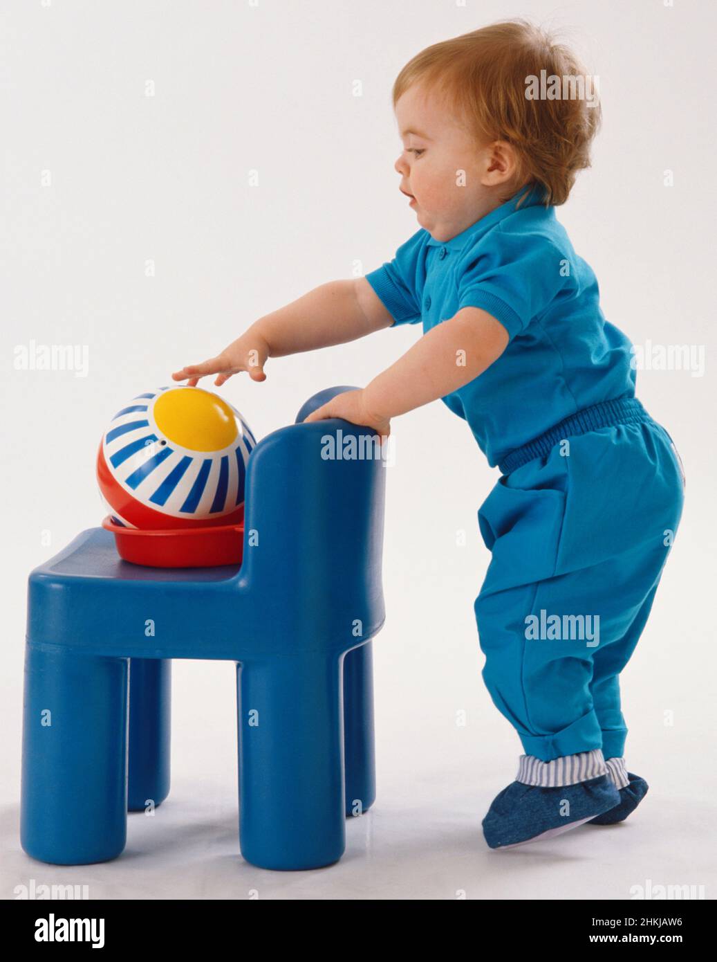 Toddler standing leaning over chairback to reach a ball Stock Photo - Alamy