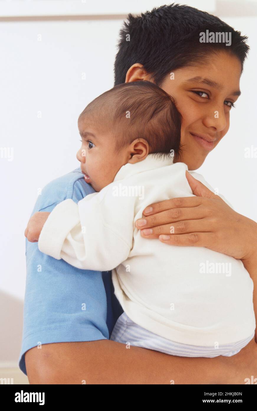 Smiling teenage boy holding a baby in a white outfit Stock Photo - Alamy