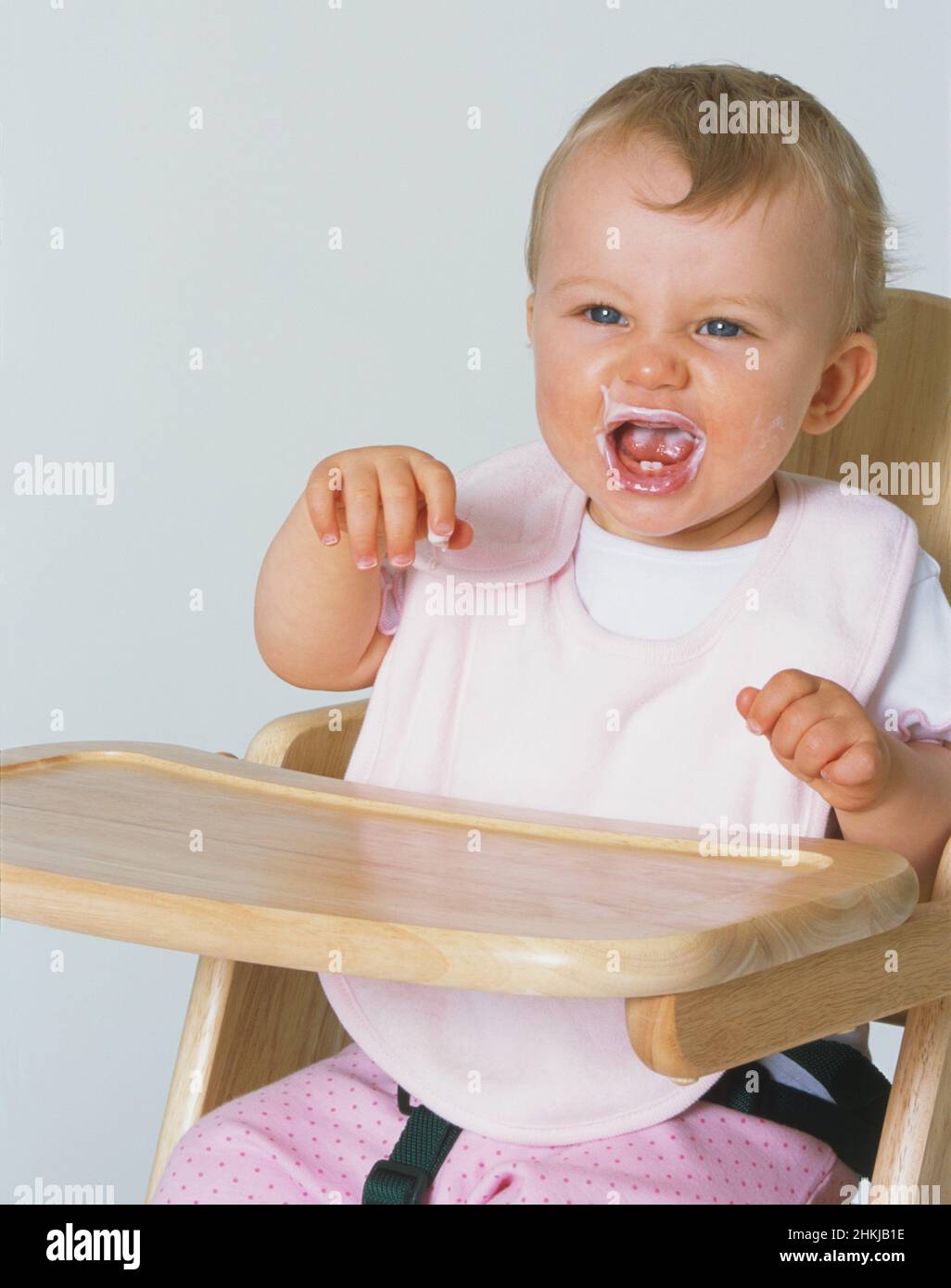 Baby girl wearing bib sitting in high chair with raised arms Stock Photo - Alamy