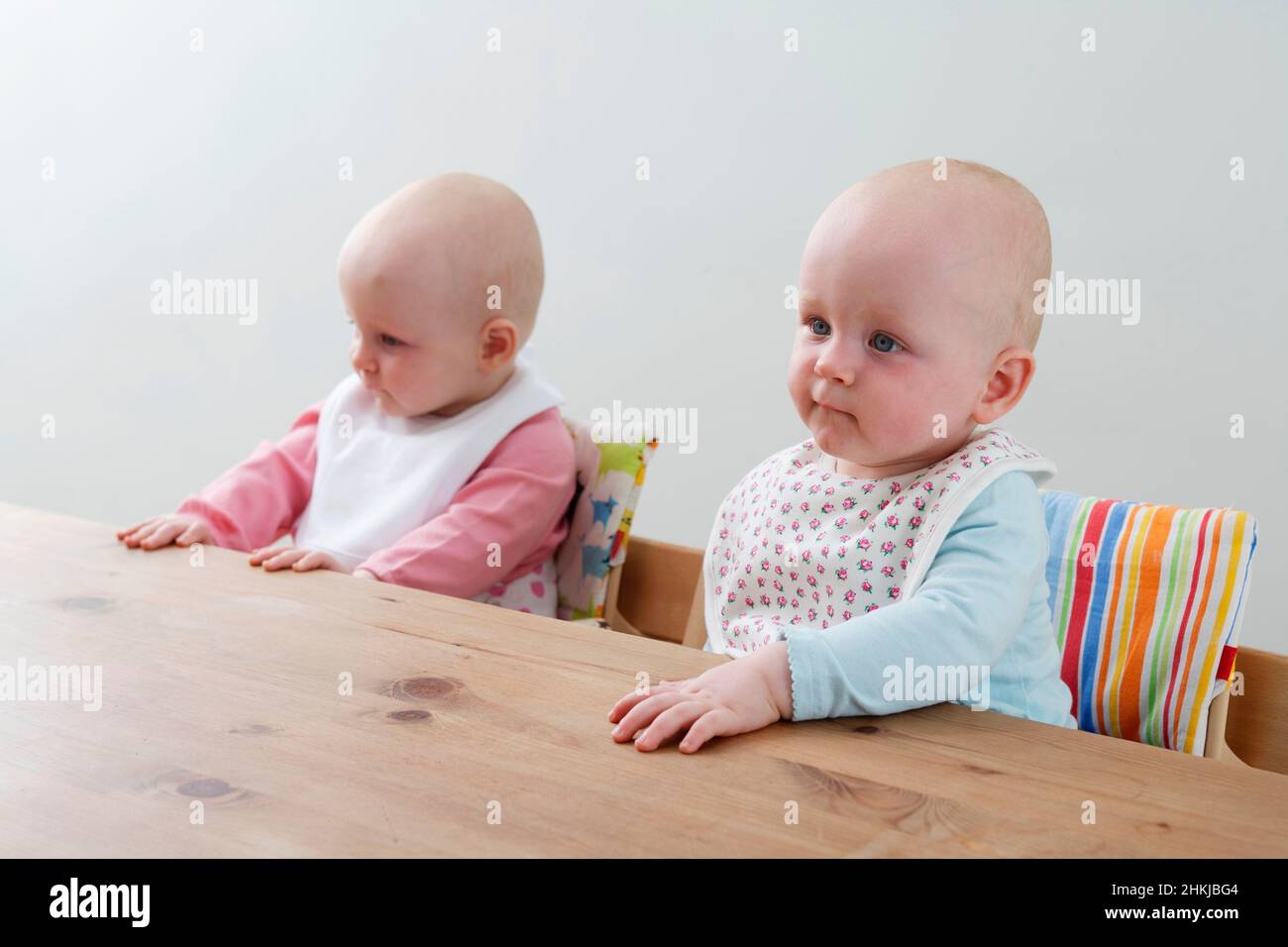 Twin babies seated in high chairs with hands on the table Stock Photo ...