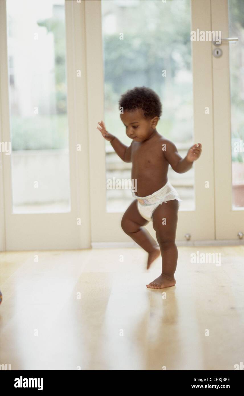 Baby boy in his nappy, raising one foot in the air, stretching out his ...