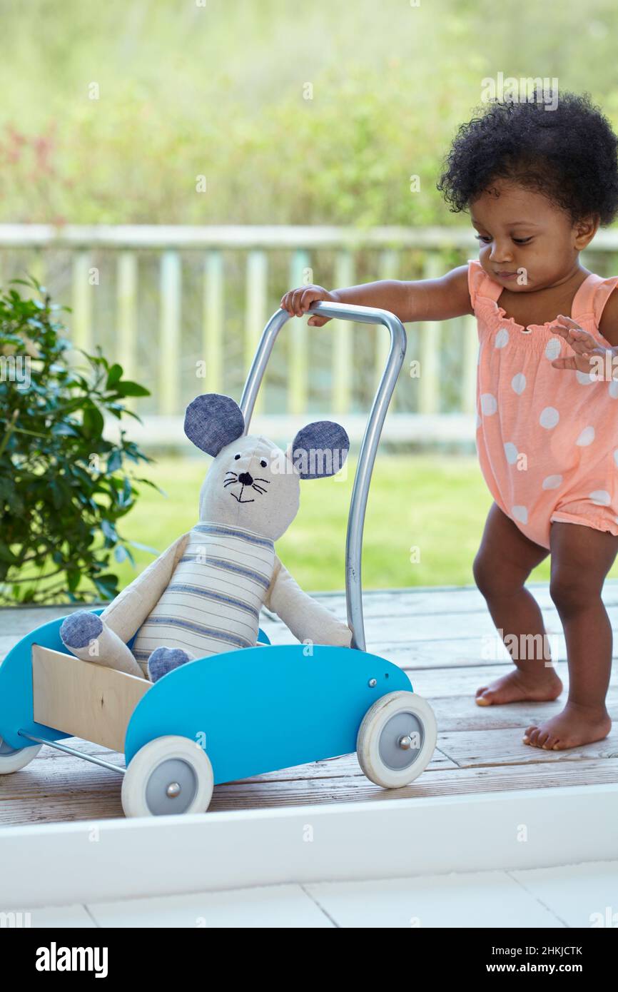 Baby girl pushing cart containing toy rabbit Stock Photo - Alamy