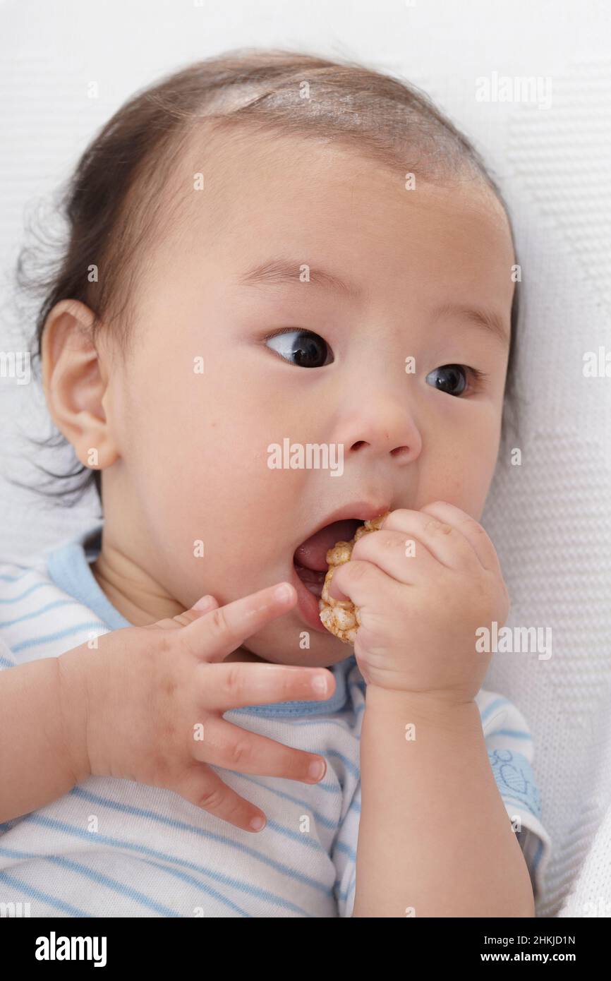 Baby boy putting rice biscuit in mouth Stock Photo - Alamy