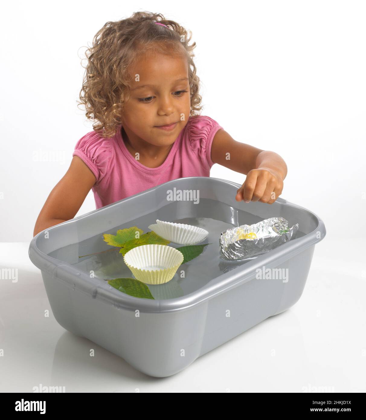 Girl looking at objects floating in washing-up bowl Stock Photo - Alamy