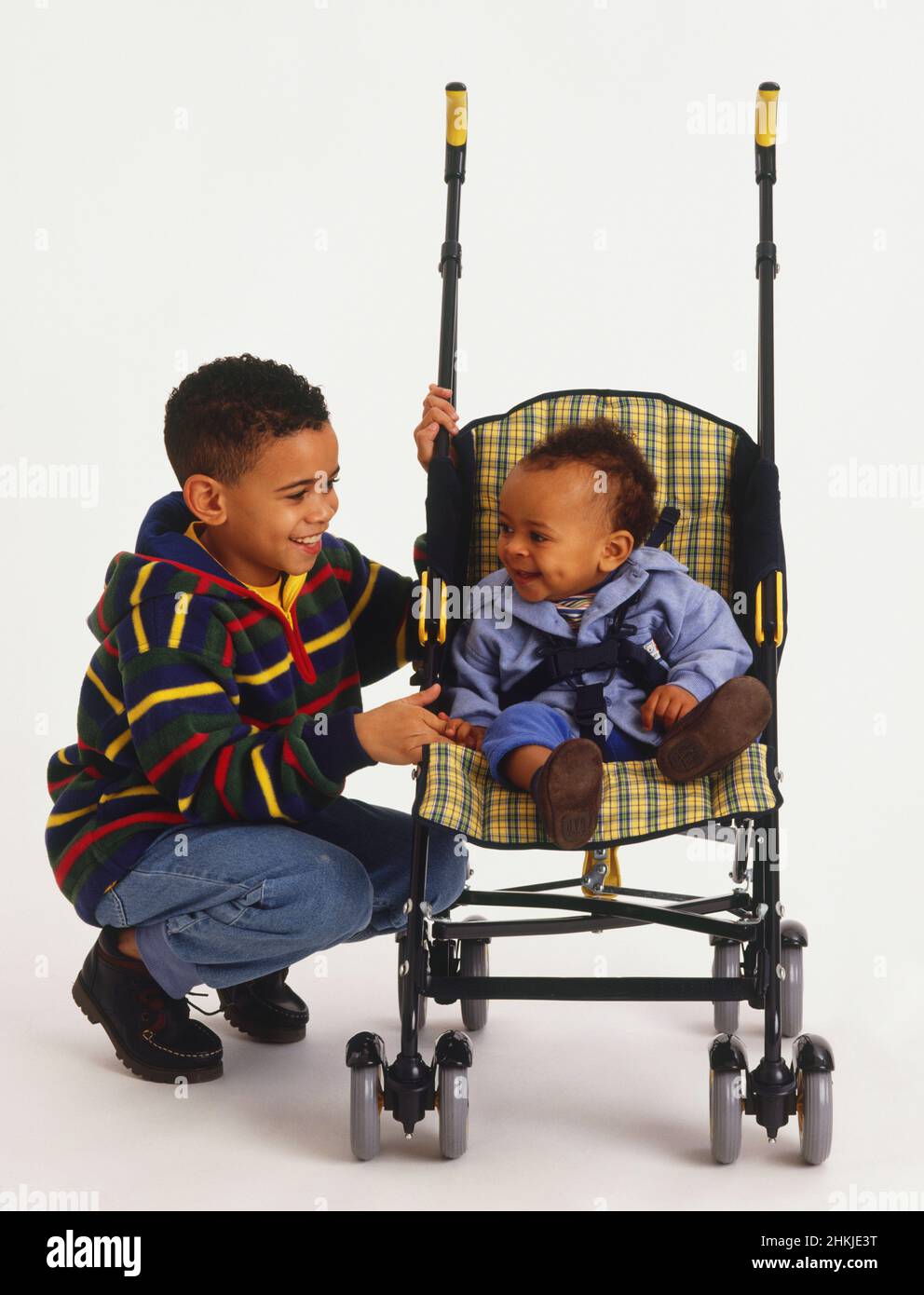 Boy crouching next to baby boy in pushchair Stock Photo - Alamy