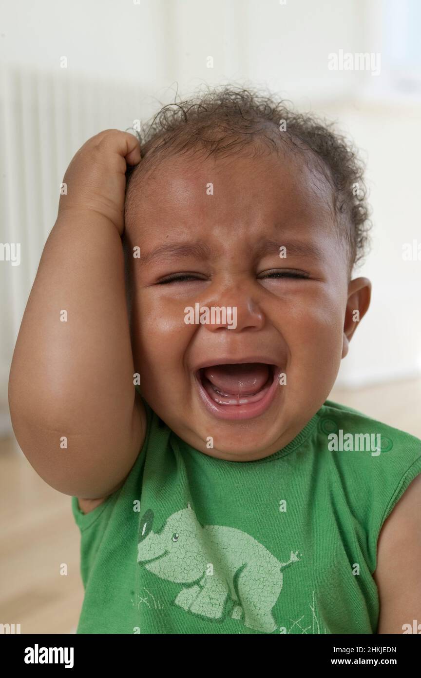 Baby boy sitting on the floor and holding his head crying Stock Photo ...