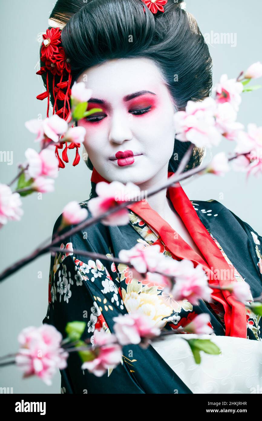 young pretty geisha in black kimono among sakura, asian ethno close up ...