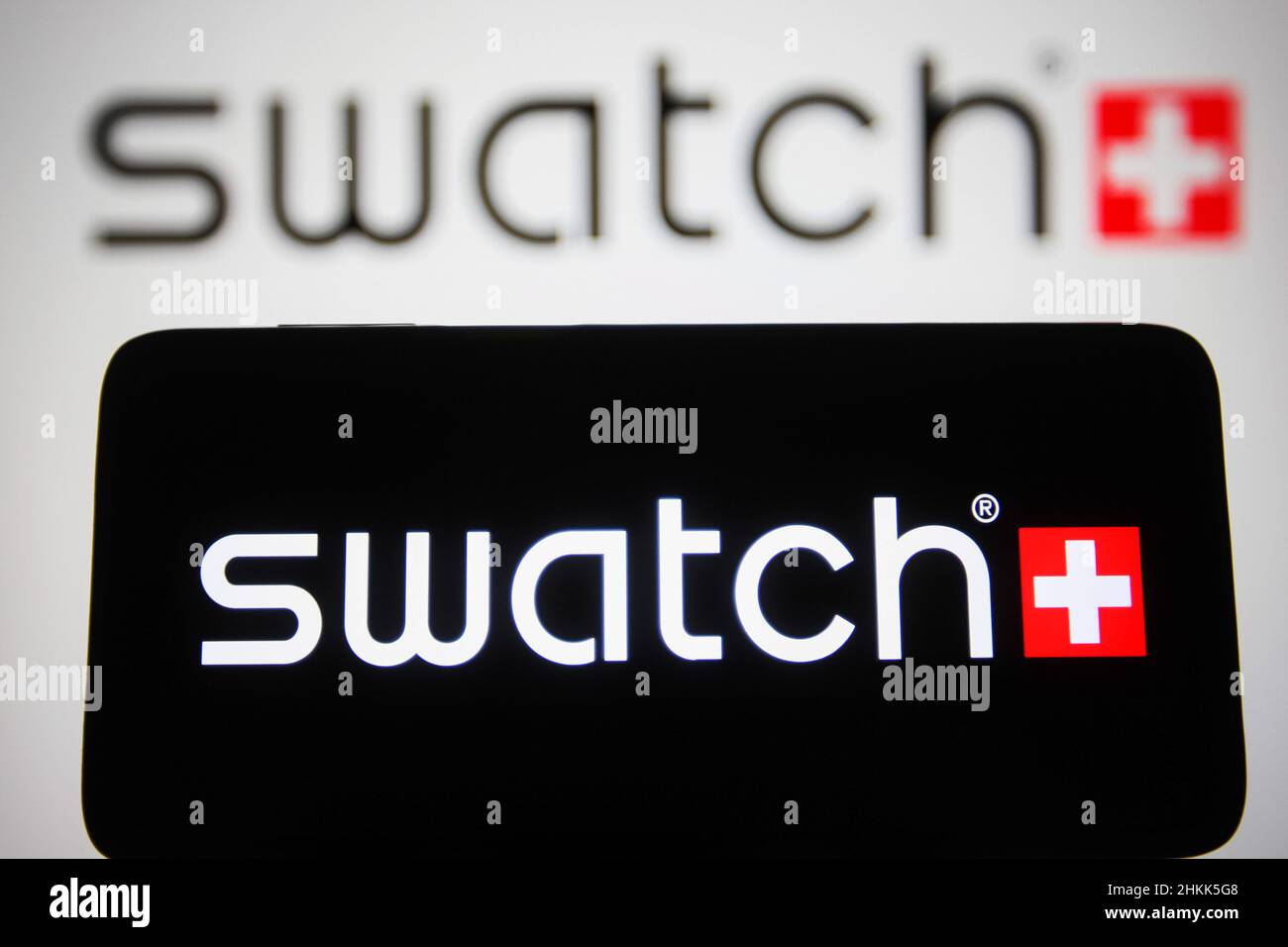 In this photo illustration, Swatch logo is seen displayed on a smartphone and in the background ...