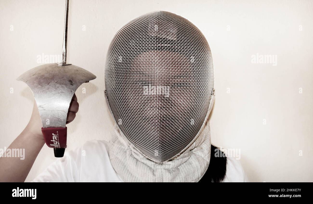A female fencer wears a mask (face shield) and holds a sword in her ...