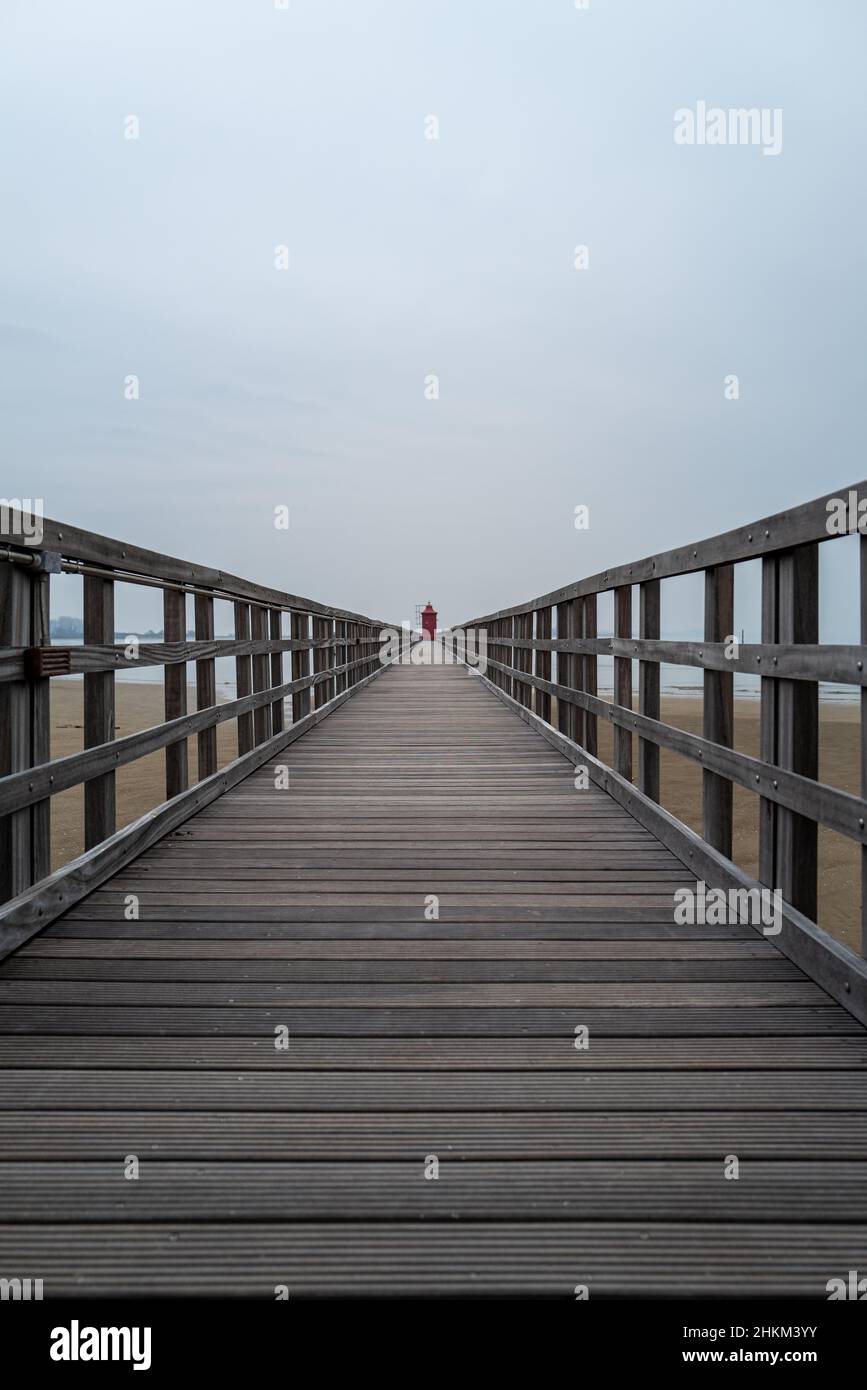 Small red old lighthouse at the end of a long jetty from a low ...