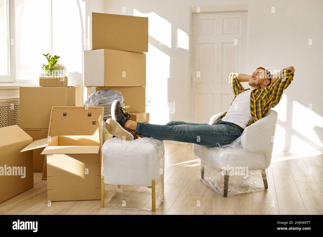 Man rest on wrapped chair among boxes Stock Photo - Alamy