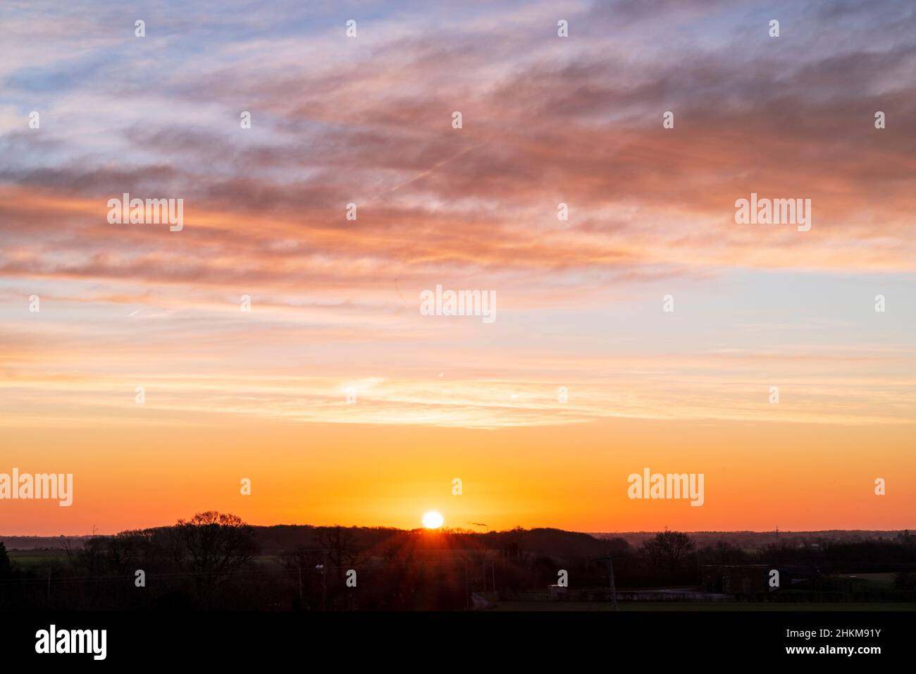 Sunrise over a flat English landscape of hedgerows and fields in the ...