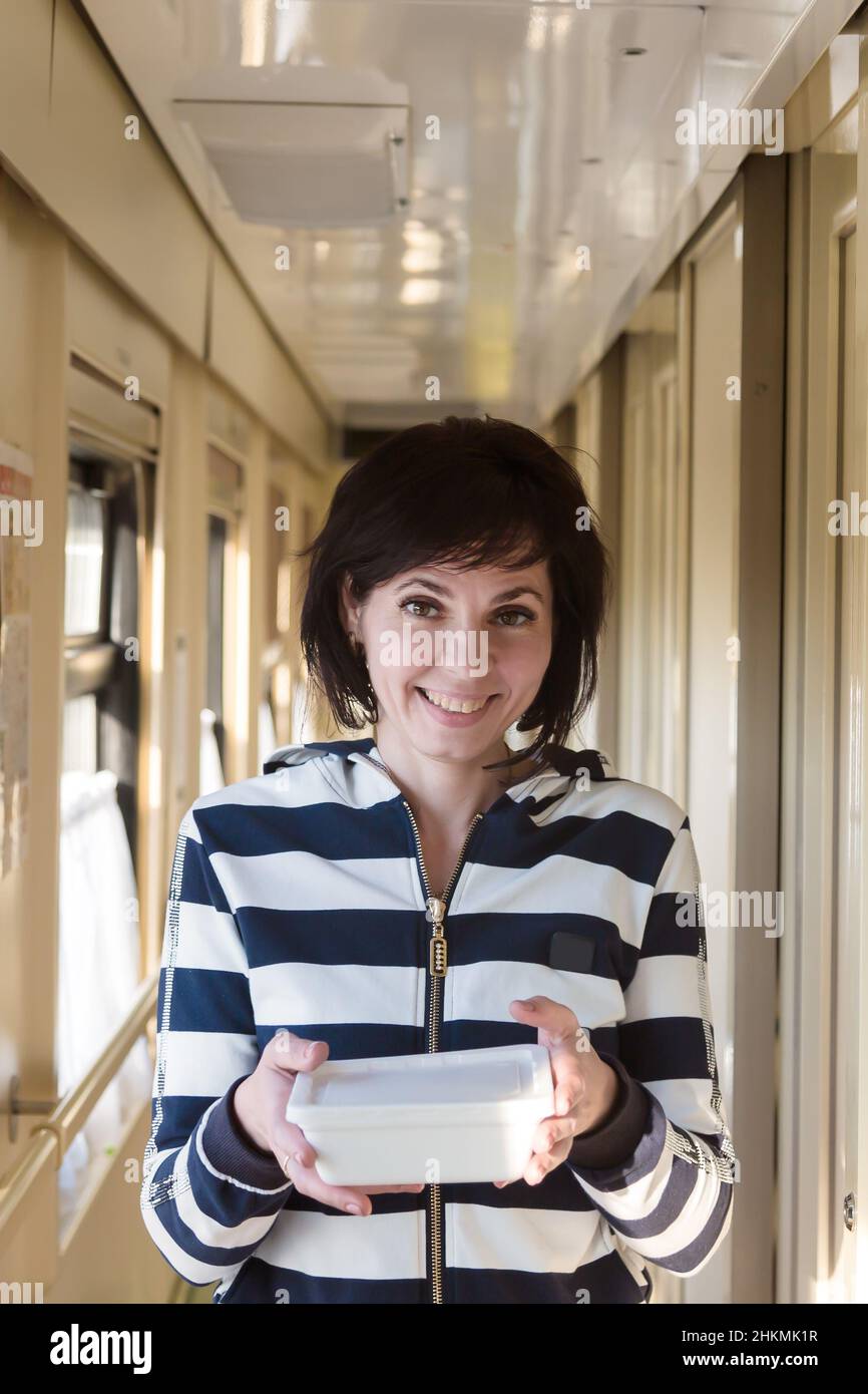 A woman smiling walks down the corridor of the train with a package of ...