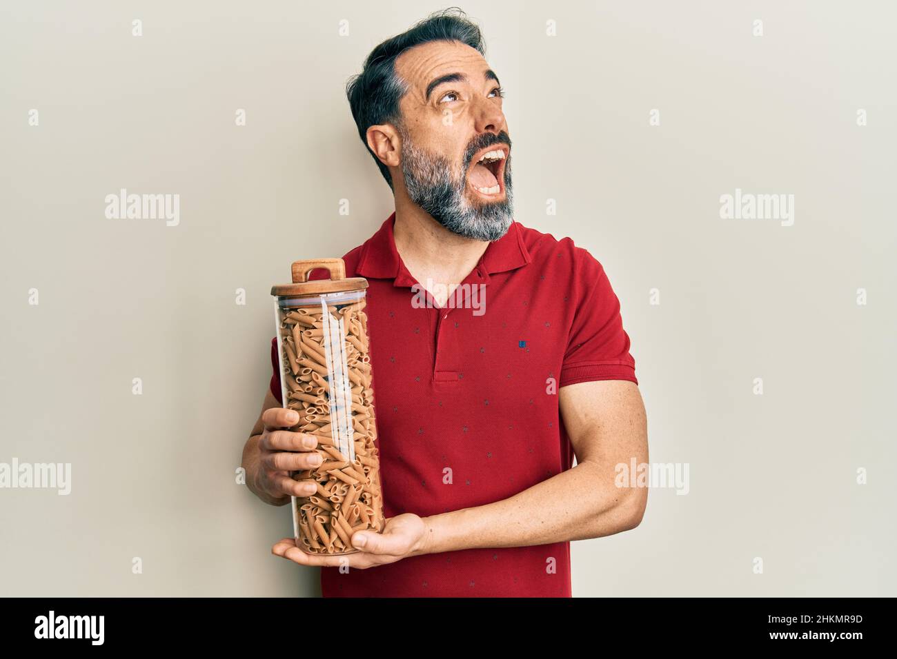 Middle age man with beard and grey hair holding jar with macaroni pasta ...