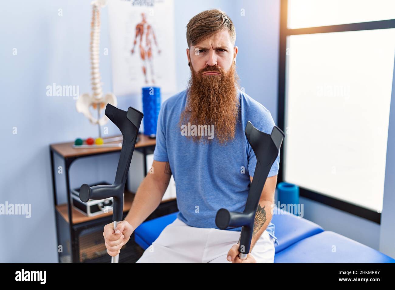 Redhead man with long beard holding crutches at rehabilitation clinic ...