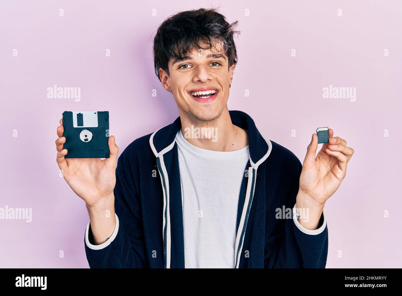 Handsome hipster young man holding floppy disk and sdxc card smiling ...