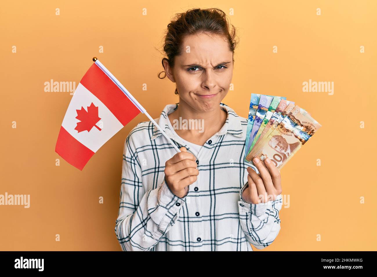 Young brunette woman holding canada flag and dollars skeptic and ...