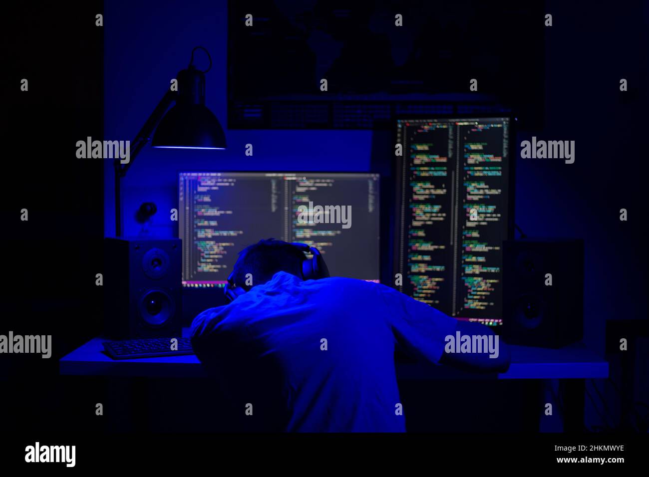 A man sleep at a computer in a room at a table at night with blue ...