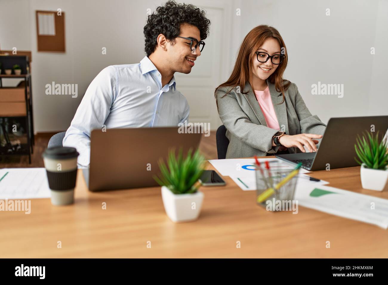 Two business workers smiling happy working using laptop at the office ...