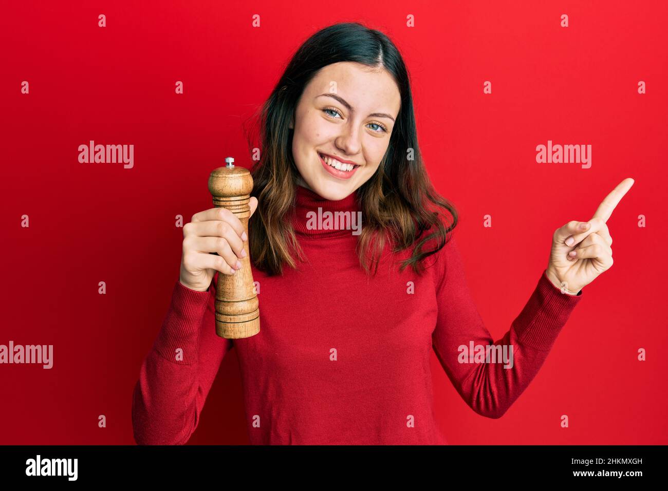 Young brunette woman black pepper grinder smiling happy pointing with ...