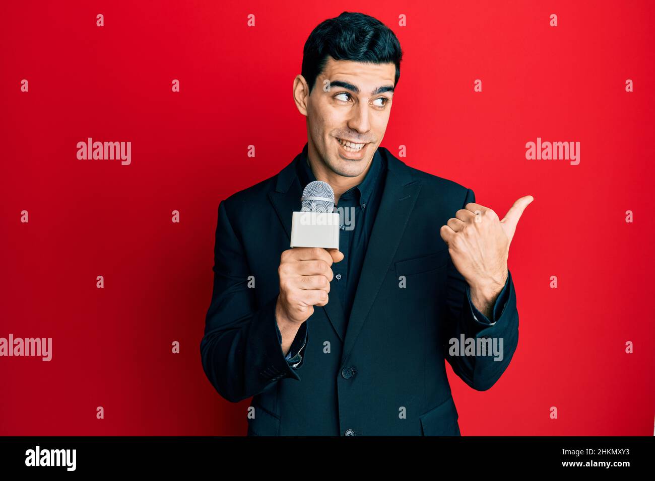 Handsome hispanic man holding reporter microphone pointing thumb up to ...