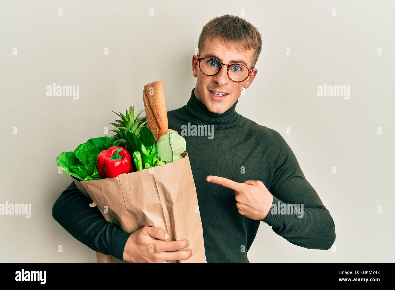 Young caucasian man holding paper bag with groceries smiling happy ... Young caucasian man holding paper bag with groceries smiling happy ...
