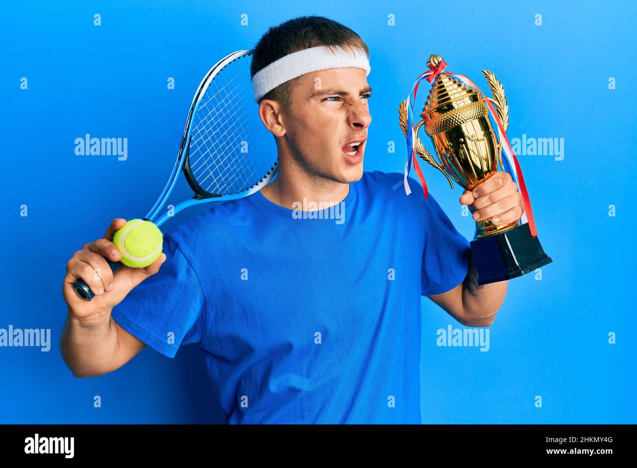 Young caucasian man playing tennis holding trophy angry and mad ...