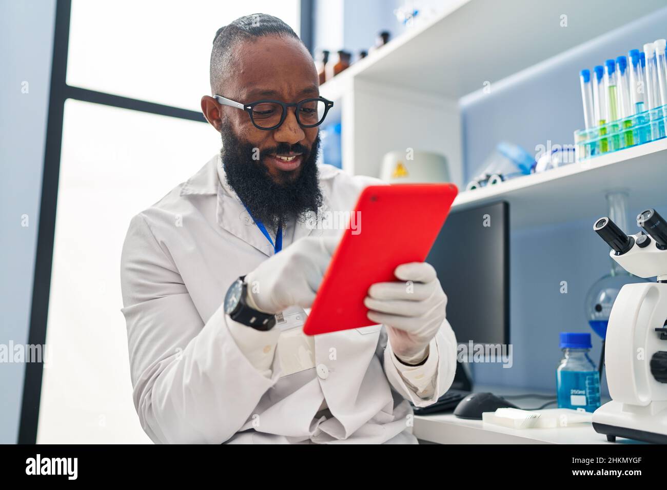 Young african american man wearing scientist uniform using touchpad at laboratory Stock Photo ...