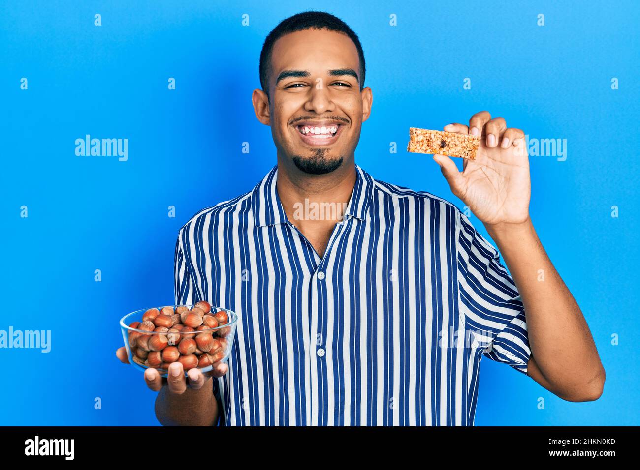 Young african american man holding raw hazelnuts and cereal bar ...