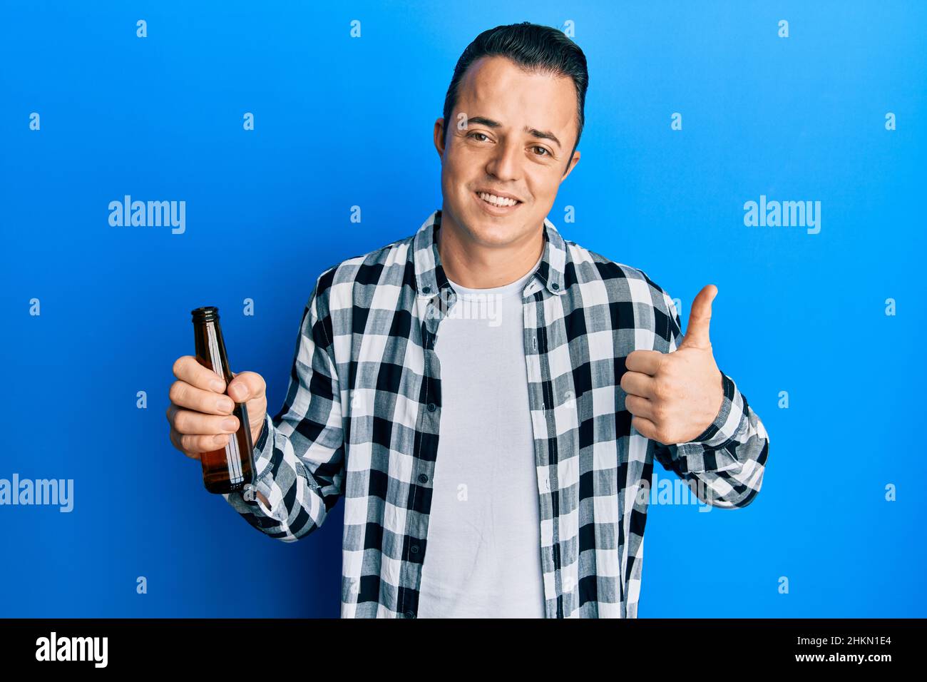 Handsome young man drinking a pint of beer smiling happy and positive ...