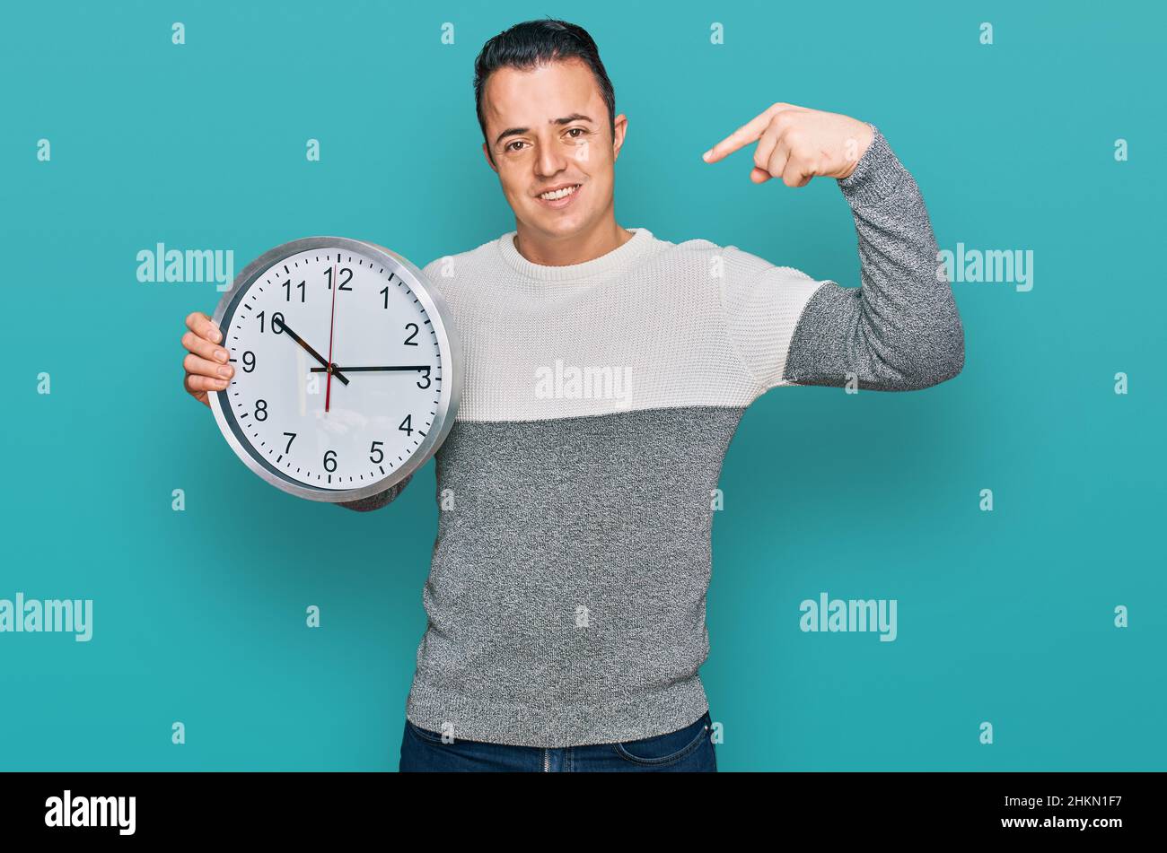 Handsome young man holding big clock pointing finger to one self ...