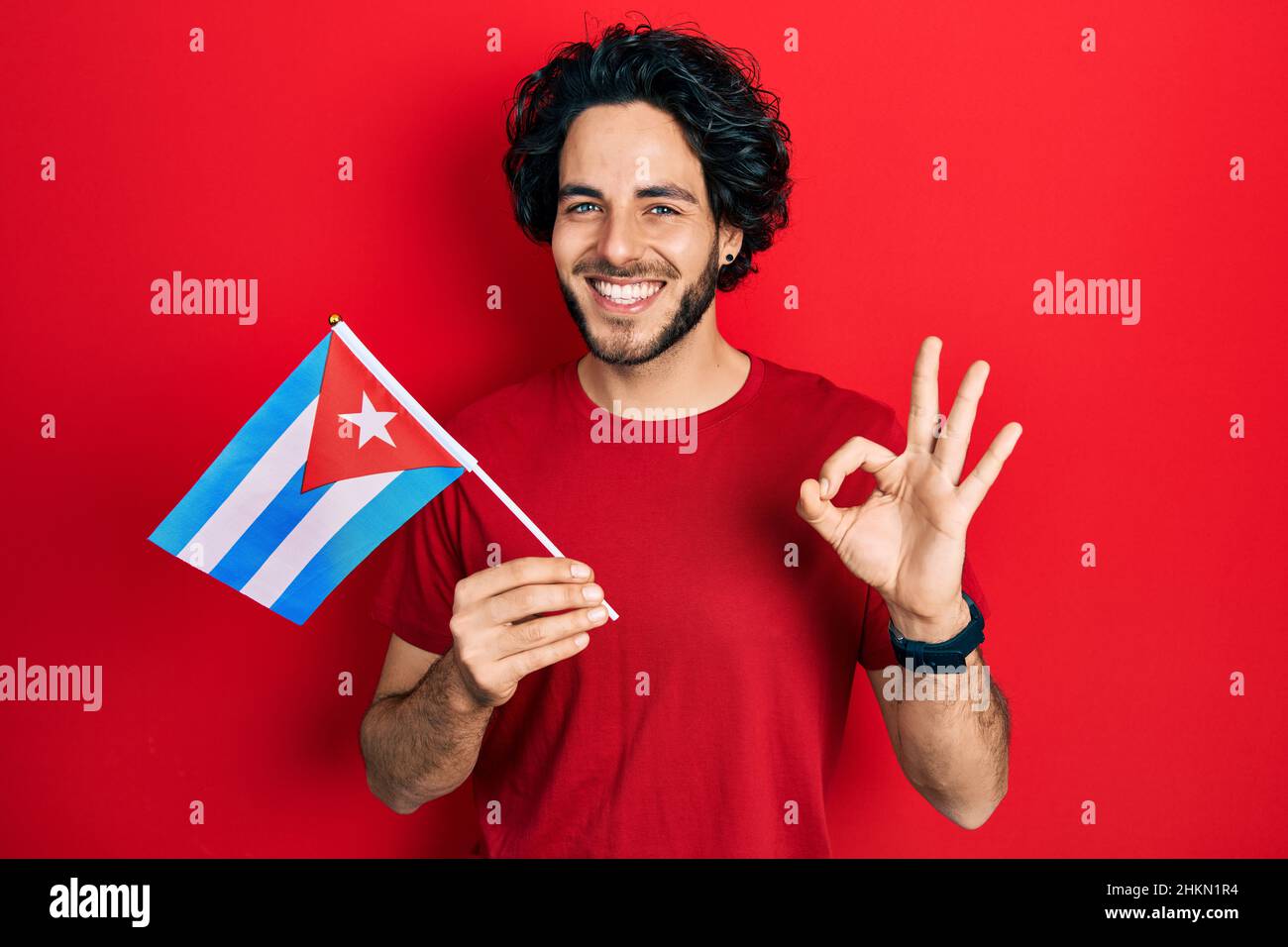 Handsome hispanic man holding cuba flag doing ok sign with fingers ...