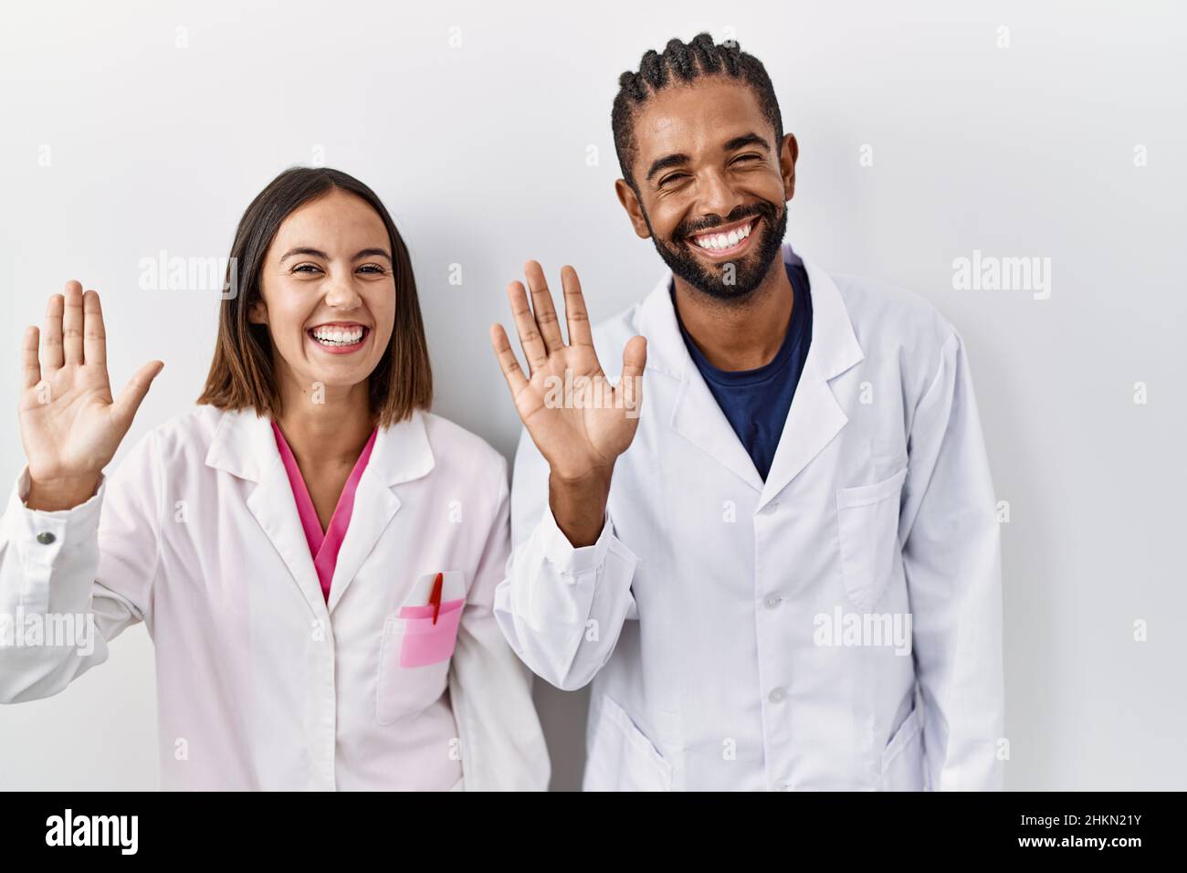 Young hispanic doctors standing over white background waiving saying ...