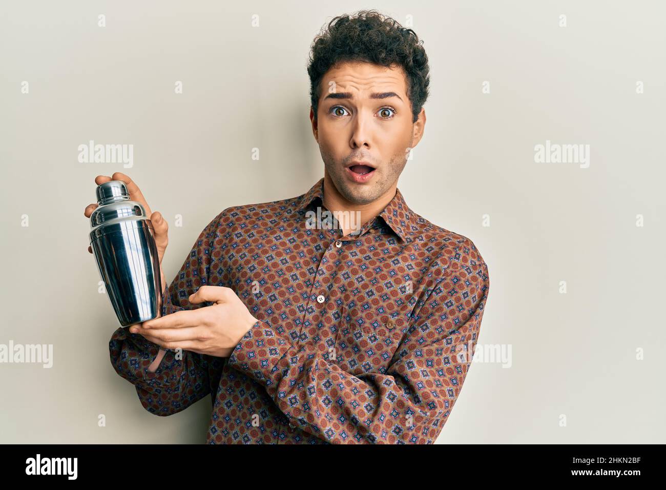 Young handsome man preparing cocktail mixing drink with shaker in shock ...