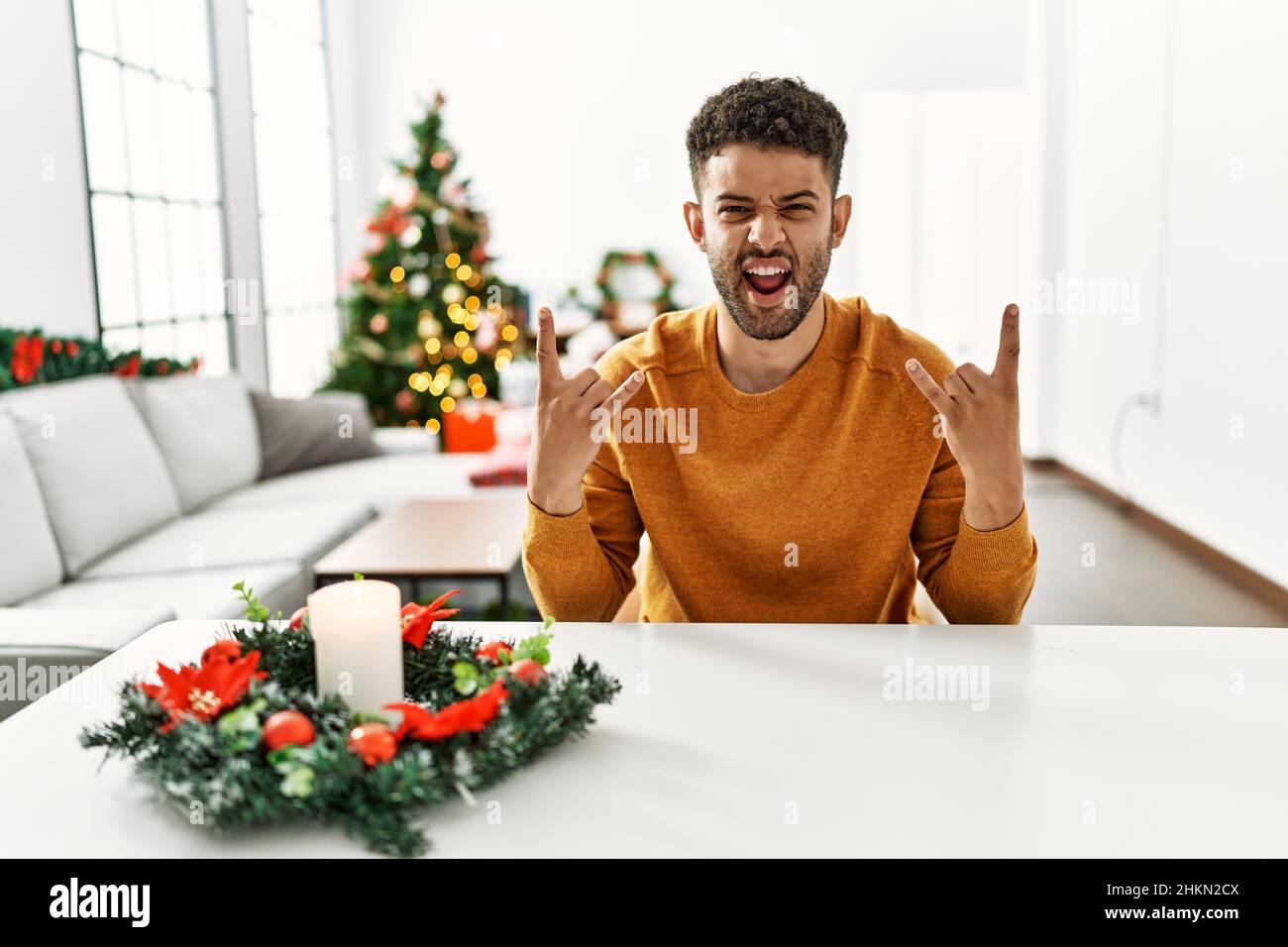 Arab young man sitting on the table by christmas tree shouting with ...