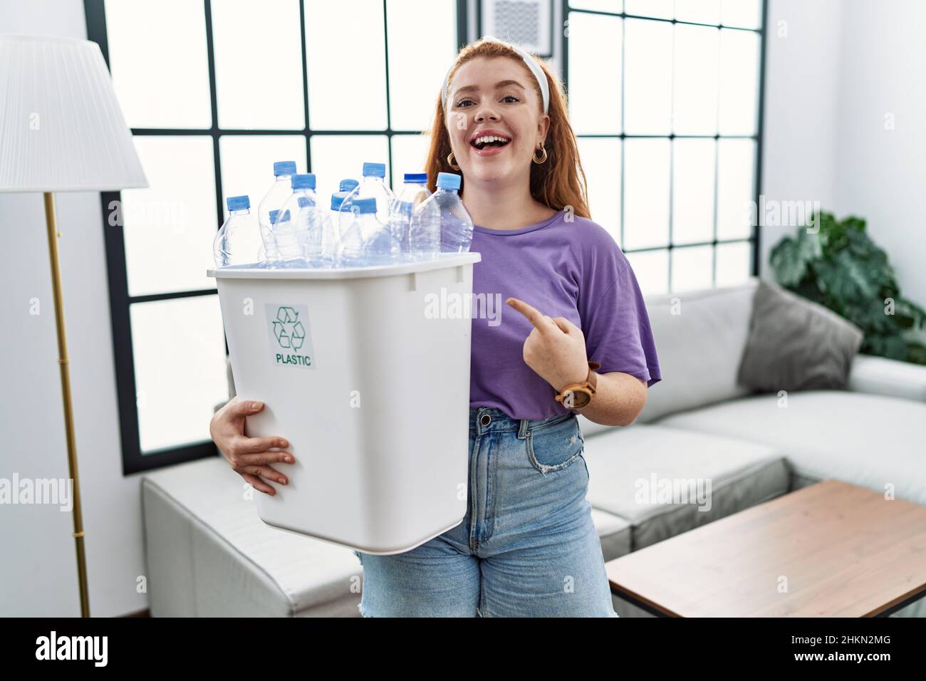 Young redhead woman holding recycling wastebasket with plastic bottles ...