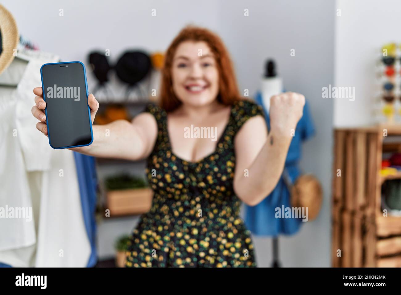 Young redhead woman at retail shop showing smartphone screen screaming ...