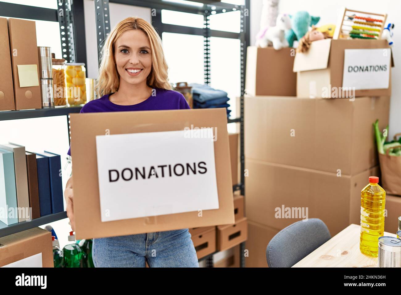 Beautiful blonde woman volunteer holding donations box smiling with a ...