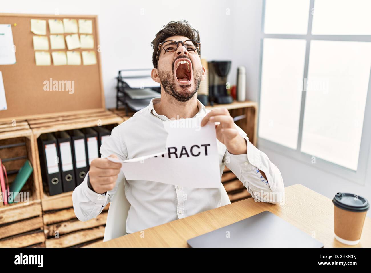 Young man with beard breaking contract paper at the office angry and ...