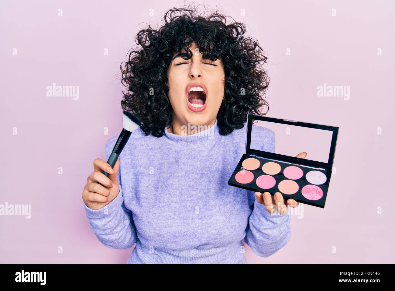 Young middle east woman holding makeup brush and blush angry and mad ...