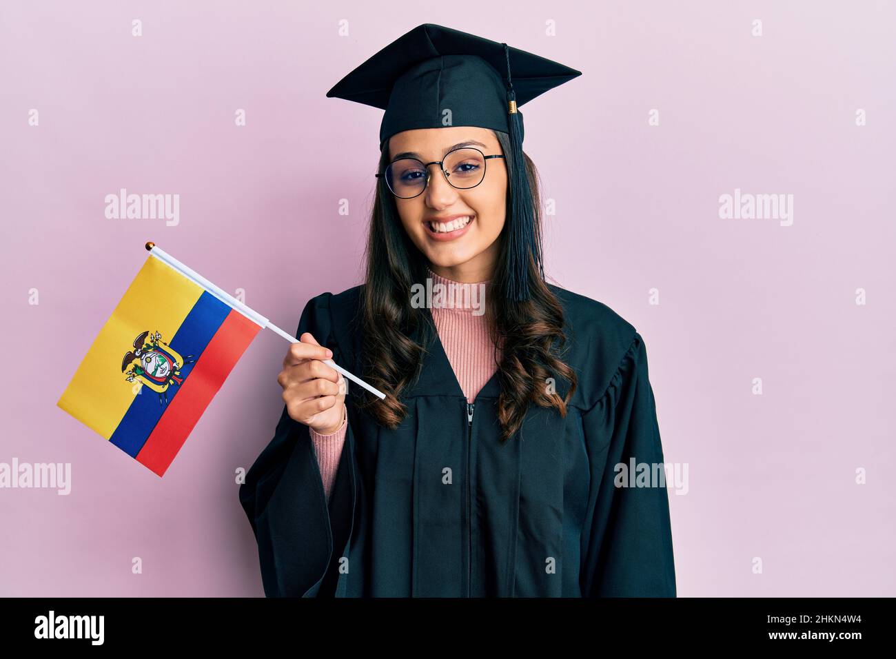 Young hispanic woman wearing graduation uniform holding ecuador flag ...