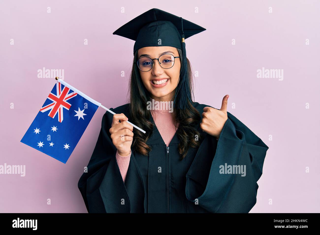 Young hispanic woman wearing graduation uniform holding australia flag ...
