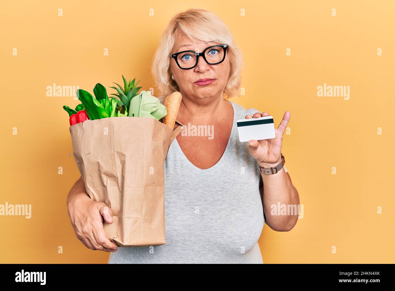 Middle age blonde woman holding groceries and credit card depressed and ...
