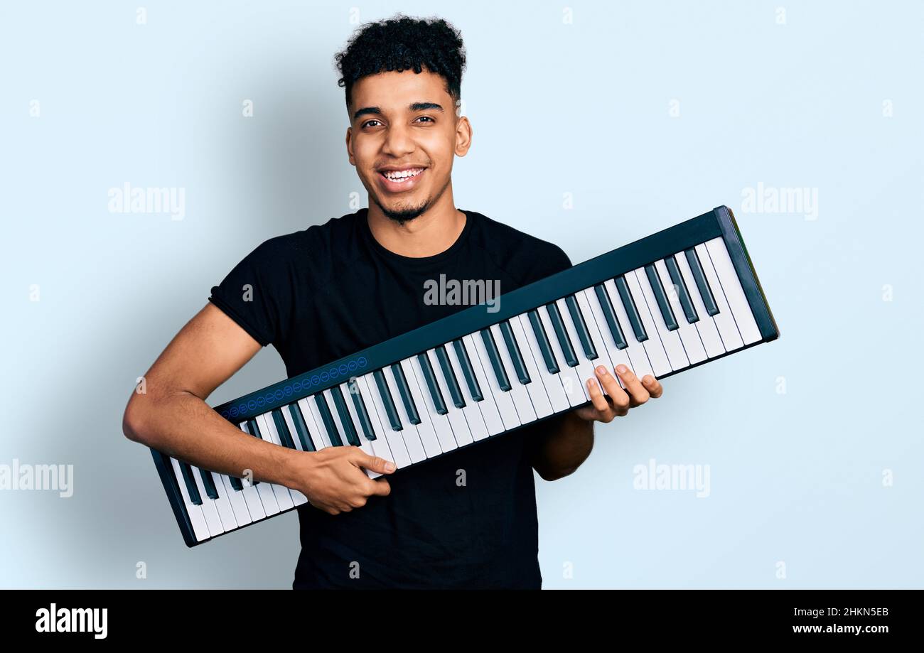 Young african american man holding piano keyboard smiling and laughing ...