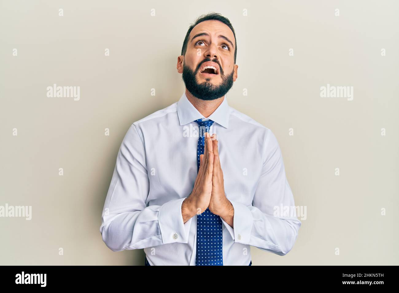 Young man with beard wearing business tie begging and praying with ...