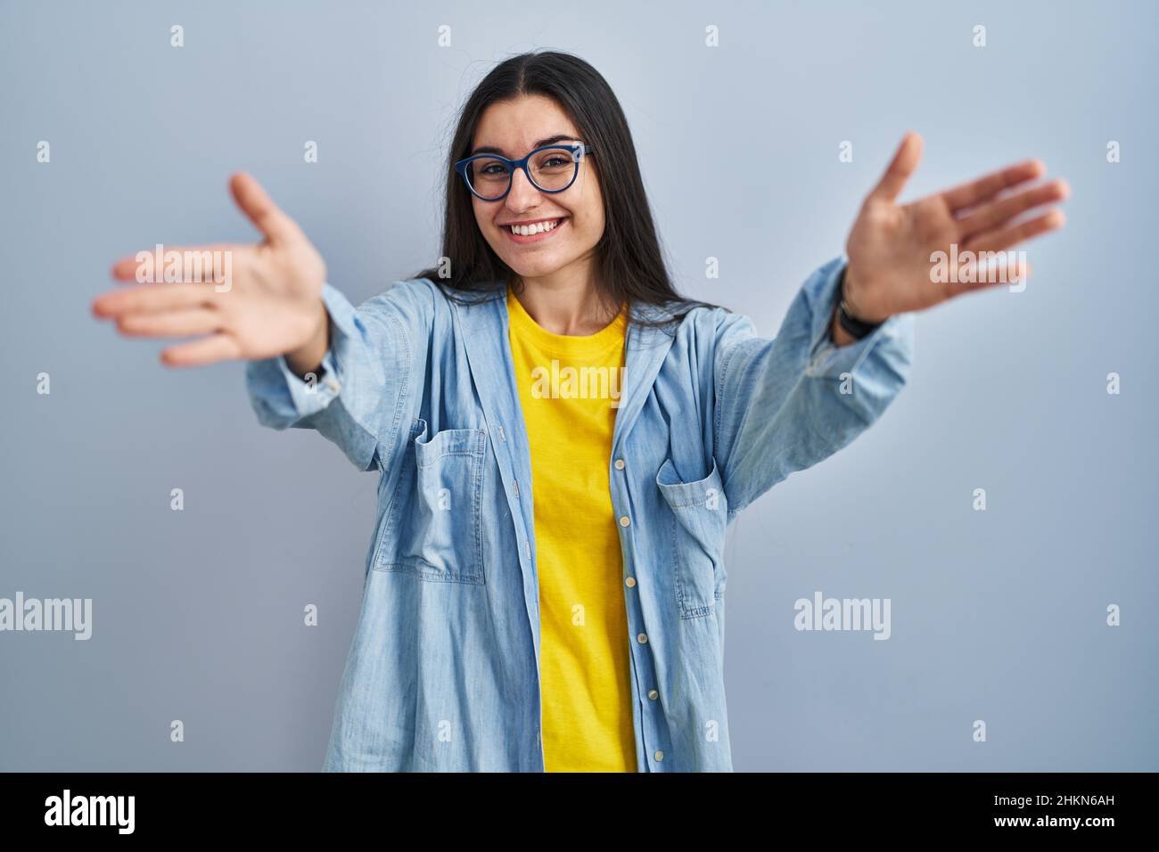 Young hispanic woman standing over blue background looking at the ...
