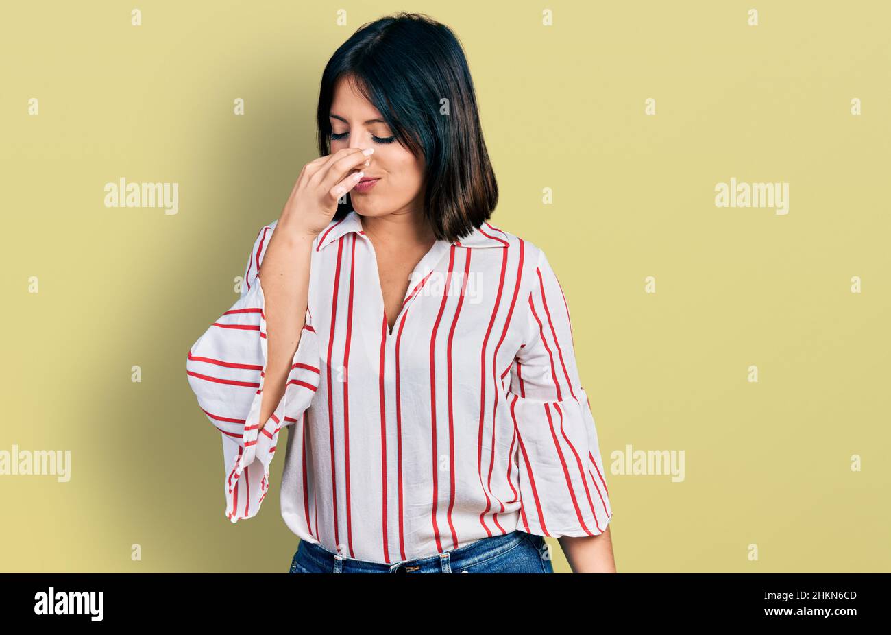 Young hispanic girl wearing casual clothes smelling something stinky ...